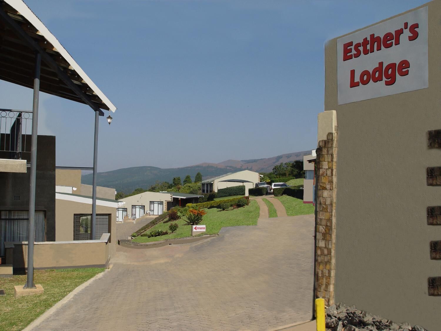 Vista da Esther's Lodge, com céu claro, um caminho de paralelepípedos até a entrada e uma placa.
