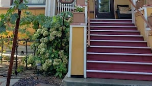 Uma casa de dois andares com varanda da frente, escada e jardim com plantas.
