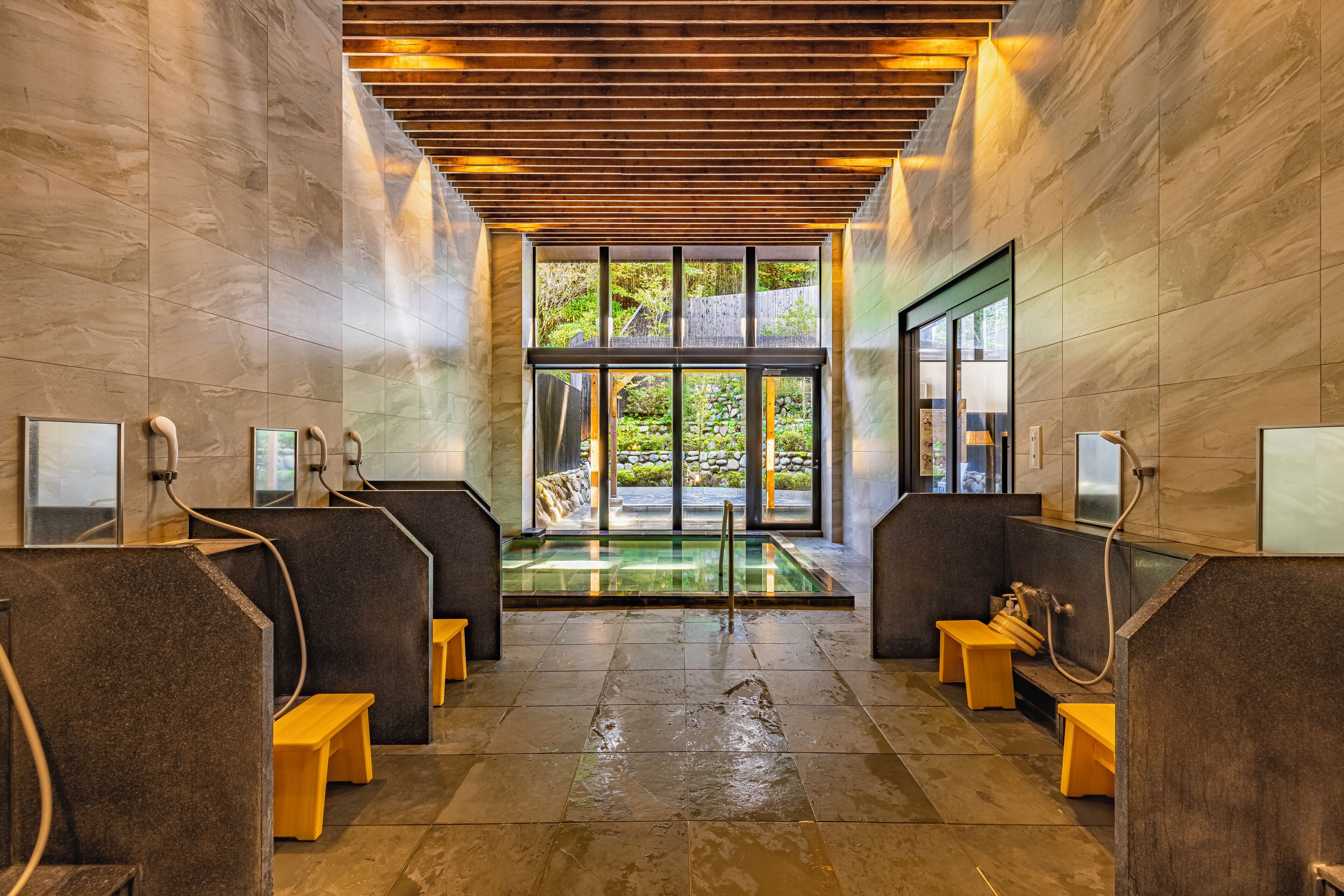 Uma área de spa moderna com paredes de pedra, bancos de madeira e uma banheira de hidromassagem em vidro.