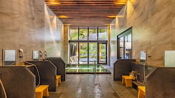 Uma área de spa moderna com paredes de pedra, bancos de madeira e uma banheira de hidromassagem em vidro.