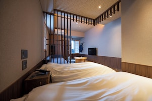 Quarto de hotel com duas camas, uma mesa pequena, televisão e escada com corrimão.