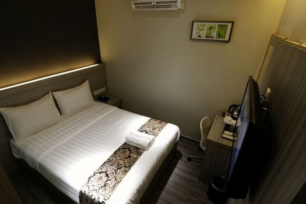 Quarto de hotel com cama, mesa de cabeceira, cadeira e televisão de tela plana.