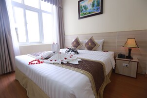 Quarto de hotel com uma cama grande, mesa de cabeceira com luminária e um quadro na parede.