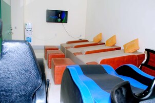 Uma sala de conferências com fileiras de cadeiras, uma televisão fixada na parede e um bebedouro.