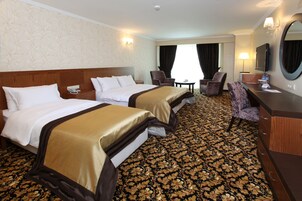 Quarto de hotel com duas camas, uma escrivaninha, uma cadeira, uma TV e um espelho grande.