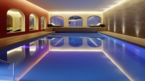 Piscina interior moderna com superfície de água azul cristalina, iluminada por iluminação ambiente.