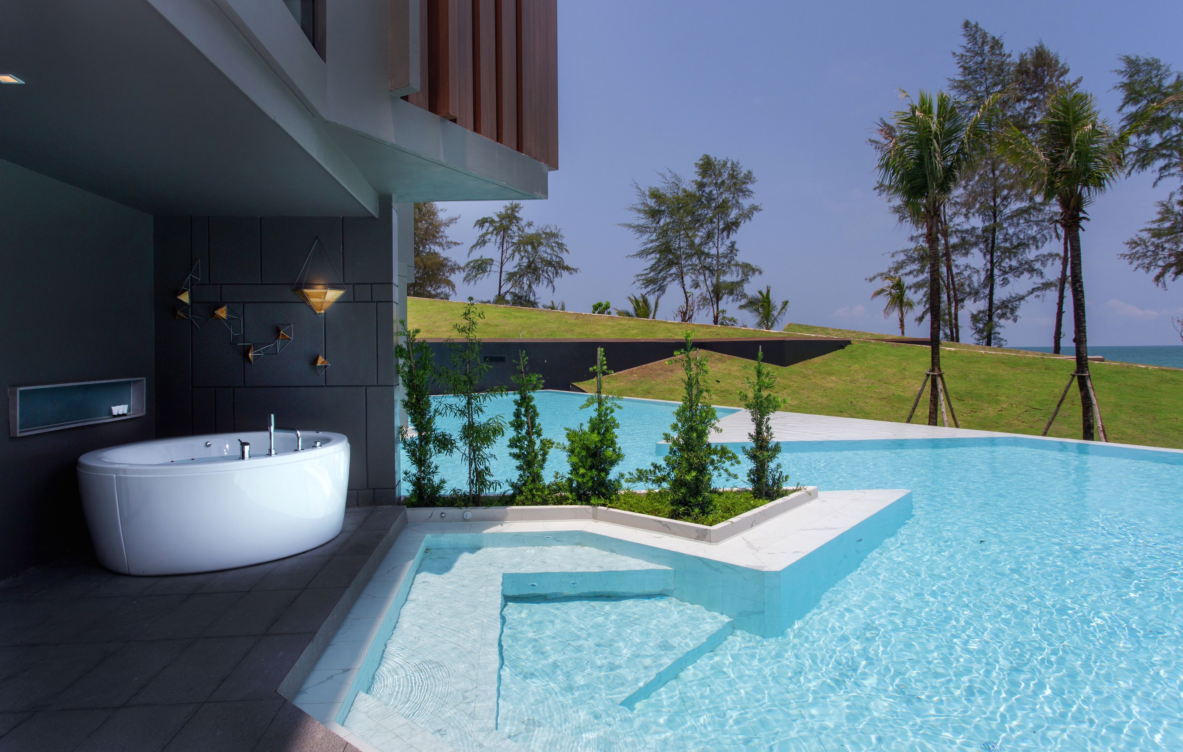 Uma área de piscina moderna com hidromassagem, água azul cristalina e vista para o oceano e palmeiras.