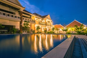 Uma piscina grande e bem iluminada com um edifício de arquitetura tradicional ao fundo.