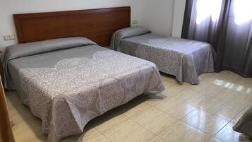 Quarto de hotel com duas camas, cabeceira de madeira, piso ladrilhado e janela com cortinas.