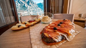 Uma mesa com dois sanduíches abertos, uma tigela de batatas fritas e vista para montanhas pela janela.