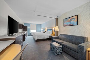 Quarto de hotel com cama, sofá, televisão e secretária.