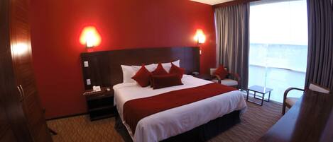 Quarto de hotel com uma cama grande, duas mesas de cabeceira, uma escrivaninha e uma cadeira.