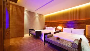 Quarto de hotel com duas camas, cabeceira de madeira, mesa de cabeceira com abajur e sofá estampado.