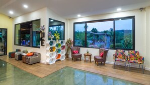 Uma sala de estar moderna com piso de madeira, um conjunto de sofás, uma estante hexagonal colorida e janelas amplas com vista para áreas verdes.