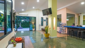 Uma sala de estar ampla, com uma janela grande, televisão de tela plana na parede, área de bar com banquetas e um balcão de recepção.