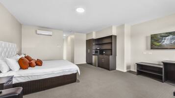 Quarto de hotel com cama, escrivaninha, televisão, área de cozinha e banheiro.