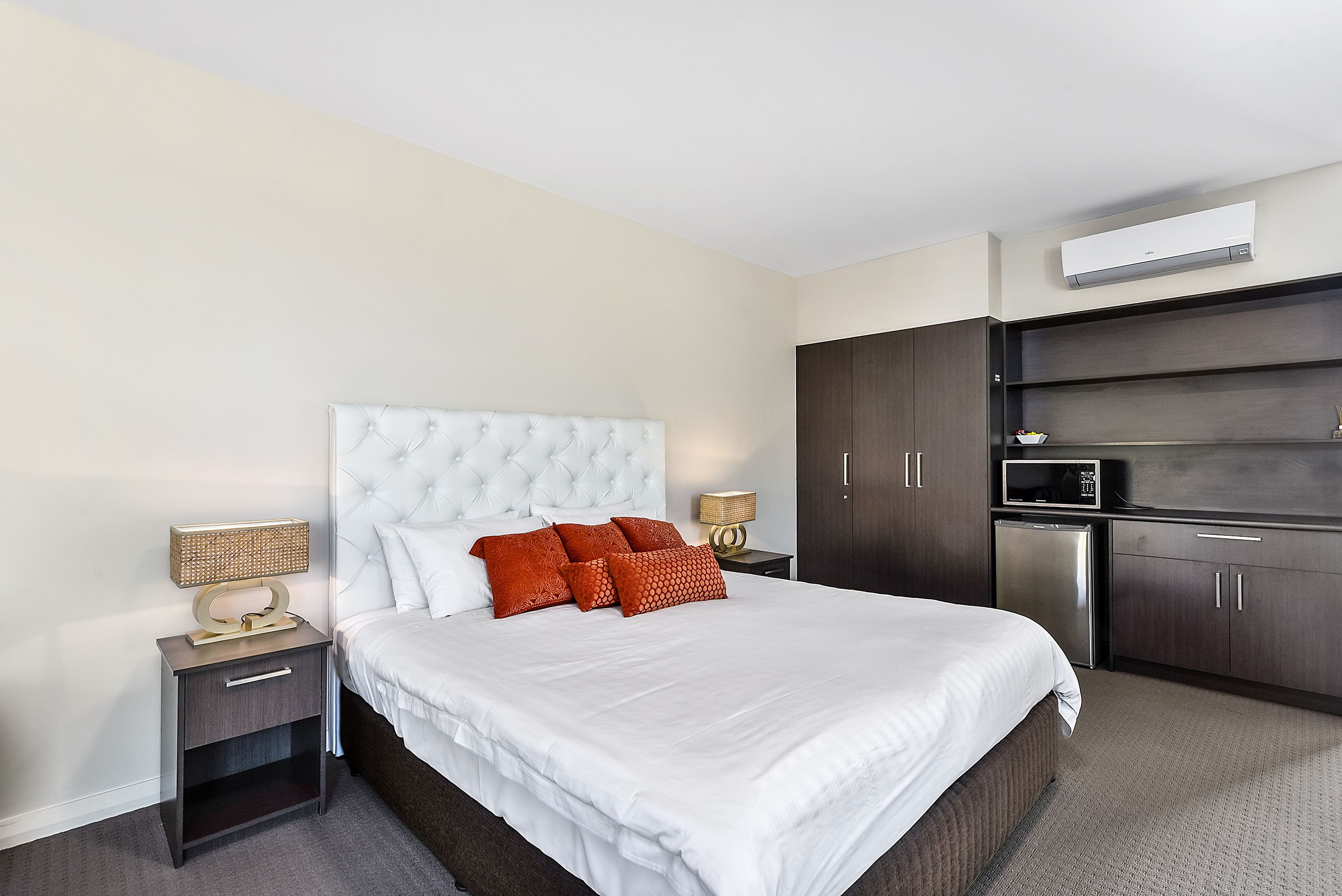 Quarto de hotel bem arrumado, com uma cama grande, mesa de cabeceira com abajur, guarda-roupa e micro-ondas embutido.
