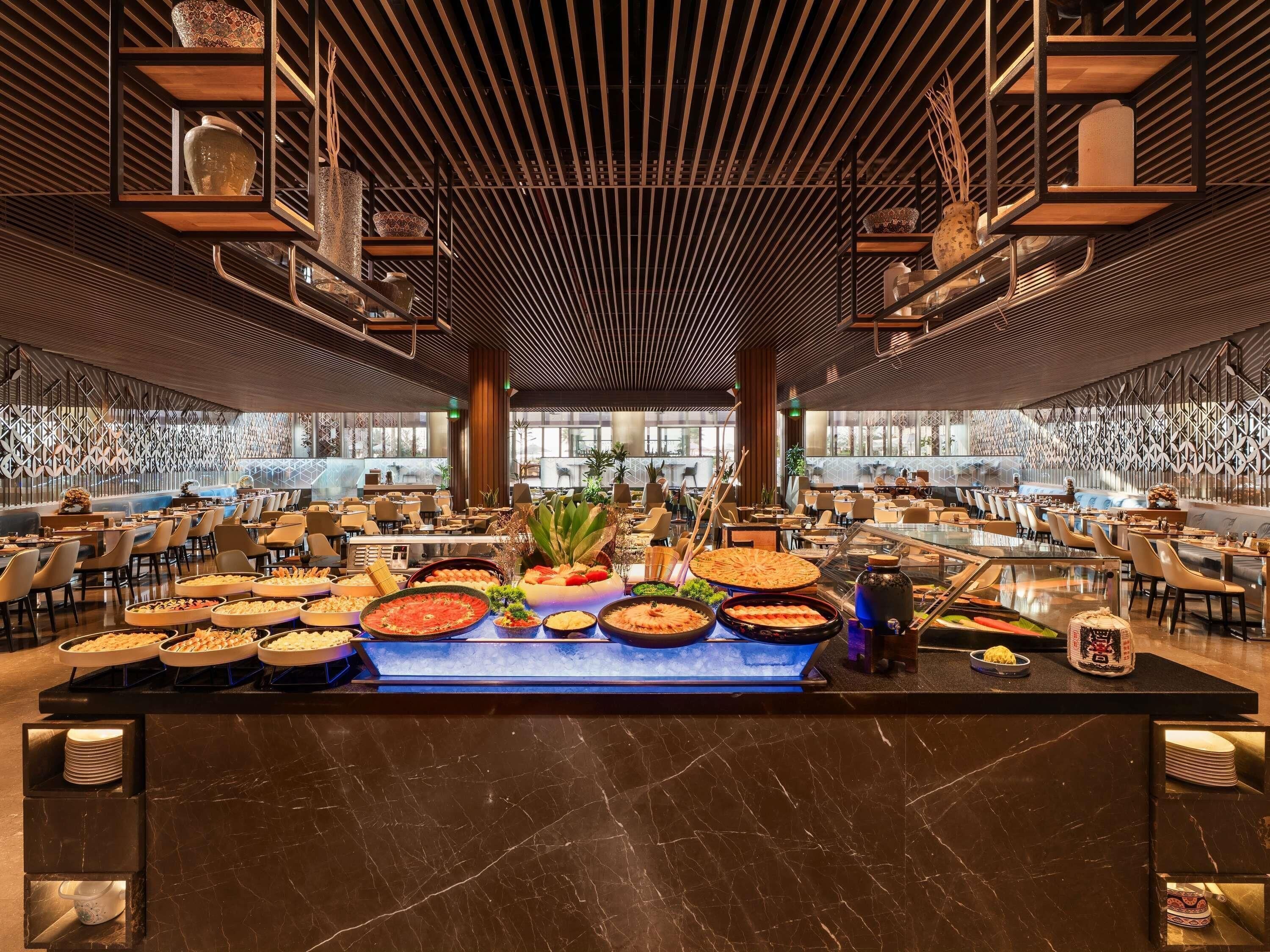 Restaurante moderno com buffet central, várias áreas de estar e teto com padrão.