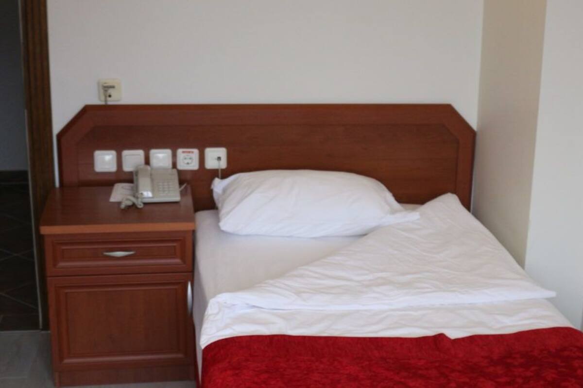 Uma cama de solteiro com cabeceira de madeira, mesa de cabeceira com telefone e um cobertor vermelho.