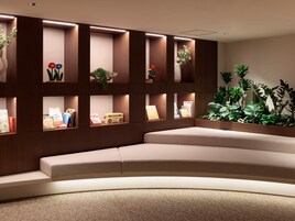 Um interior moderno com um sofá curvo, estantes de madeira com diversos objetos e plantas em vasos.