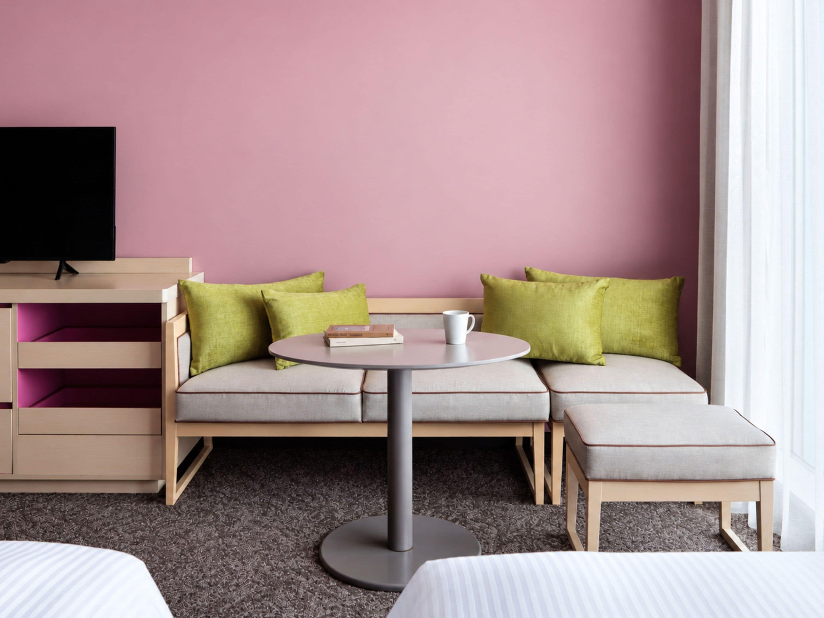 Quarto de hotel moderno com sofá modular, mesa redonda e televisão.