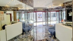Um hall de hotel moderno com piso de mármore, divisórias de vidro e áreas de estar.