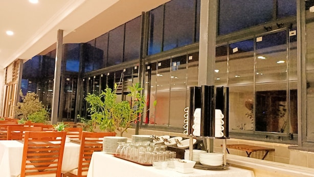 Um restaurante com mesas compridas, cadeiras e uma área de buffet com pratos e copos.