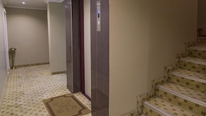 Um corredor com carpete estampado, uma porta e uma escadaria.