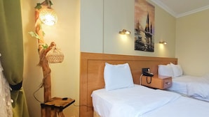 Quarto de hotel com cabeceira de madeira, cama com roupa de cama branca, mesa de cabeceira com telefone e luminária fixa na parede.