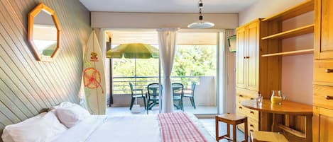 Um quarto com uma cama, um guarda-roupa de madeira, uma mesinha com cadeira, e uma varanda com mesa e cadeiras.