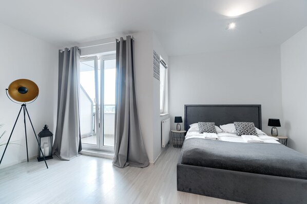 Quarto moderno com uma cama grande, uma luminária de chão e vista para o exterior.