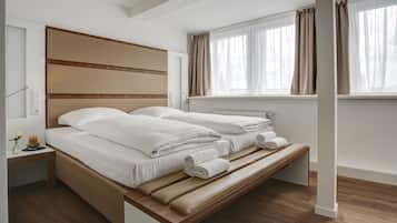 Quarto de hotel moderno com uma cama grande, uma mesinha de cabeceira com abajur e uma janela com cortinas.