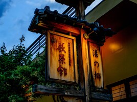 Uma placa de madeira japonesa tradicional com caracteres, fixada numa estrutura de madeira com telhado de telhas.