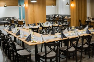 Restaurante com longas mesas de madeira preparadas para refeições, cadeiras pretas e design de interiores moderno.