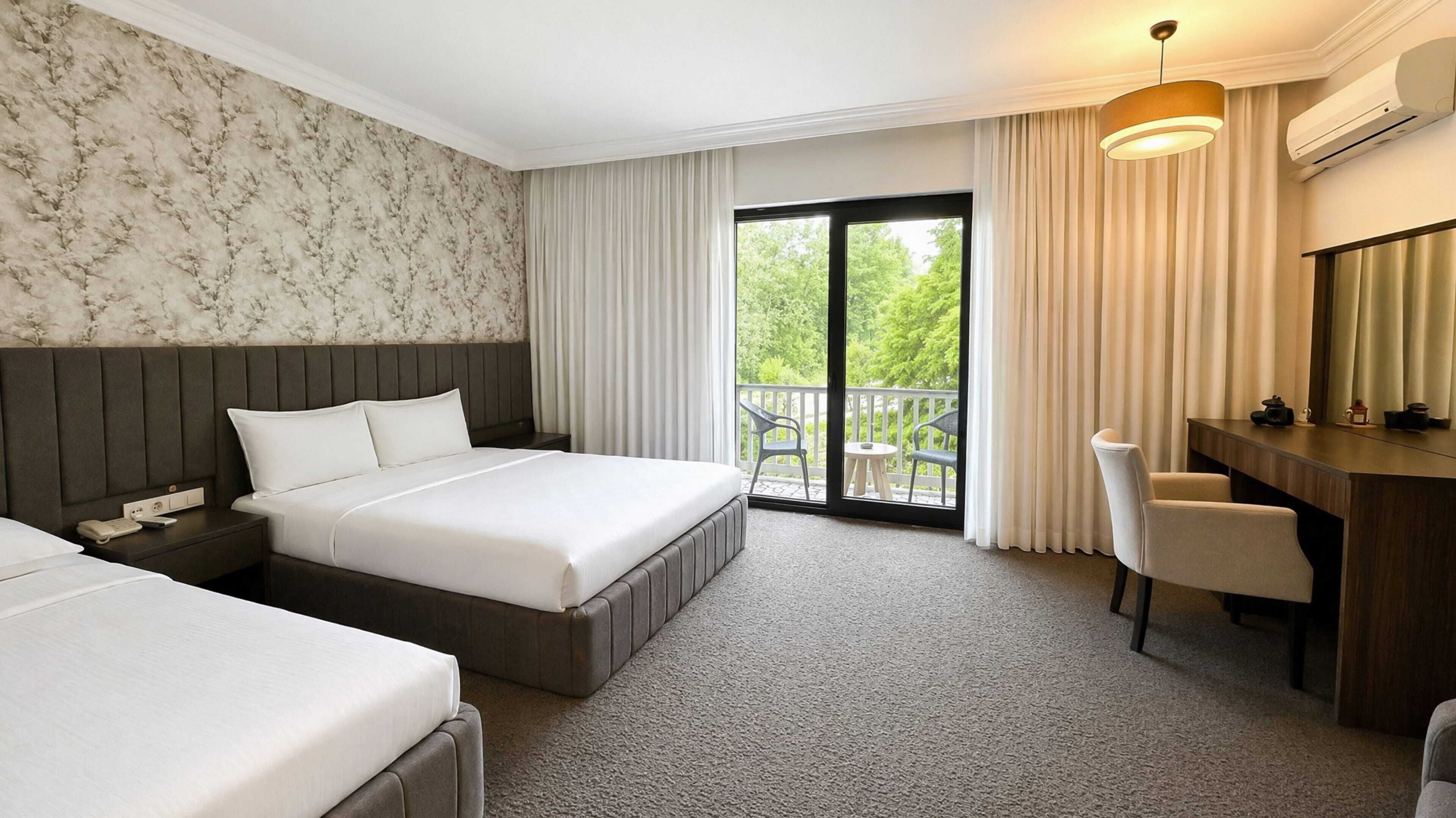 Quarto de hotel com cama, escrivaninha, cadeira e varanda com vista para o verde.