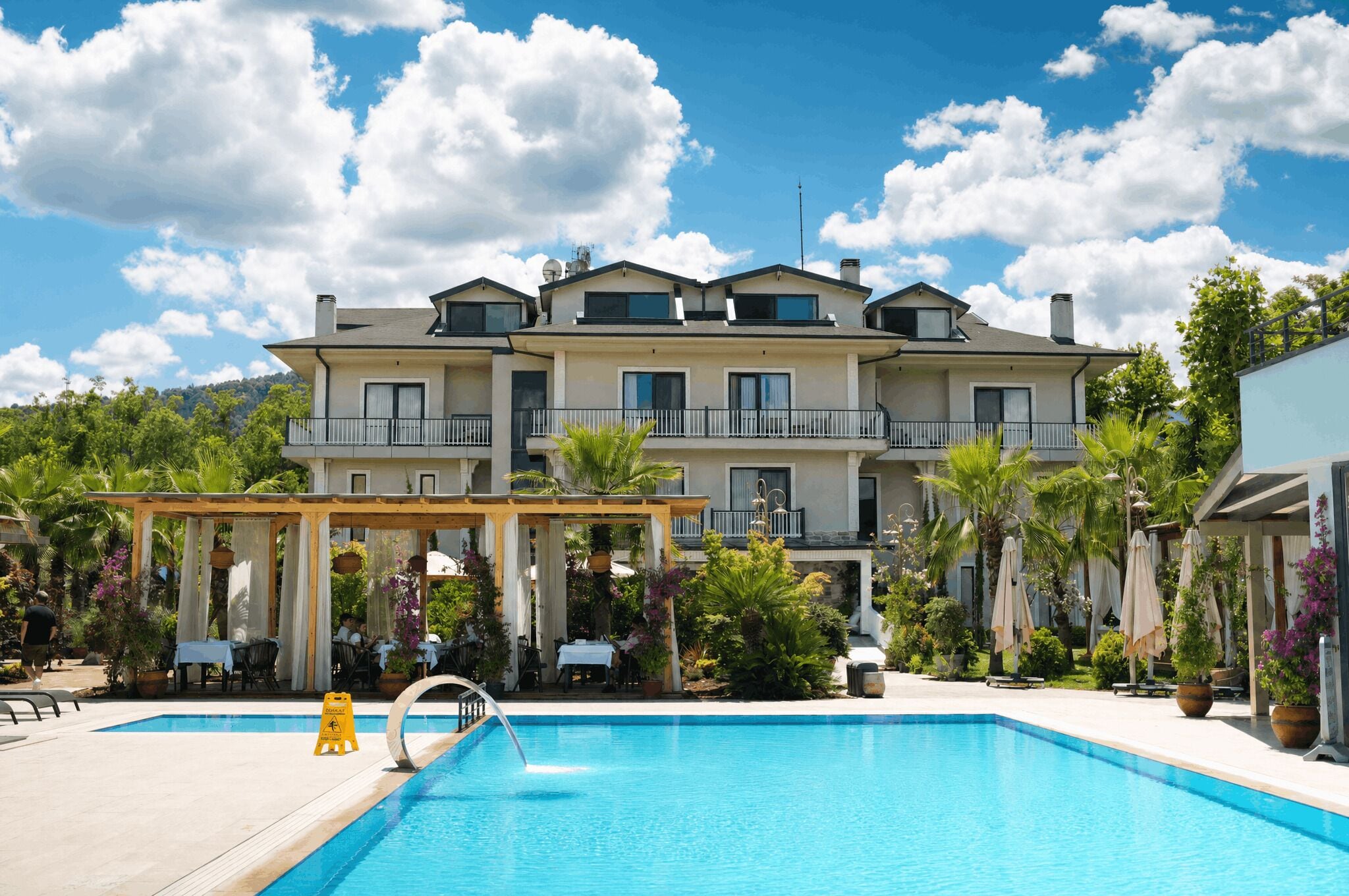 Um hotel com piscina, área de estar ao ar livre e um edifício grande com várias varandas.