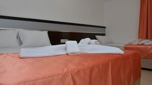 Quarto de hotel com duas camas, cada uma com cabeceira branca, colchas laranjas e toalhas brancas dobradas com capricho.