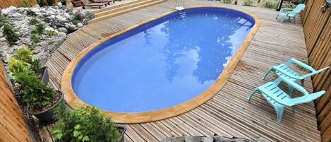 Um deck de madeira com piscina, rodeado por plantas em vasos e mobiliário de exterior.