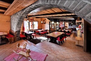 Um interior rústico em madeira, com paredes de pedra, mesas de madeira e cadeiras estofadas em vermelho.