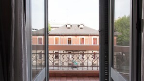 Vista de uma varanda com grade de metal, um edifício com telhado de telhas e céu claro.