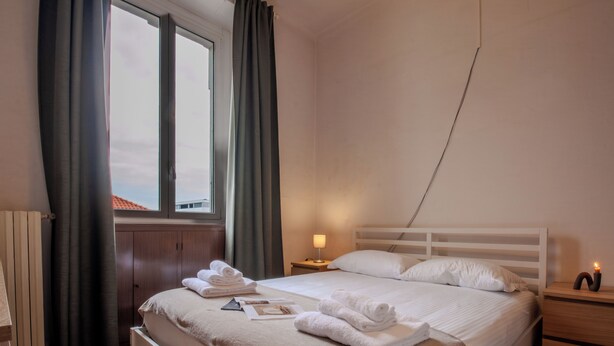 Cama arrumada com toalhas, abajur e mesa de cabeceira.