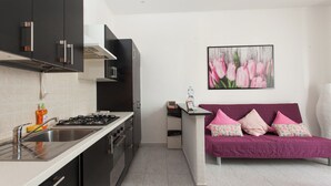 Uma cozinha moderna com armários pretos, eletrodomésticos de aço inoxidável e um sofá roxo com almofadas estampadas.