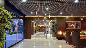 Um hall de hotel moderno com piso lustroso, painéis de madeira e uma grande janela com vista para a rua.