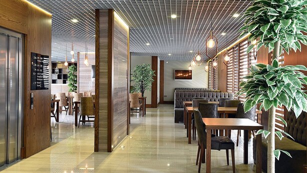 Interior moderno de restaurante com teto em padrão quadriculado, detalhes em madeira e diferentes opções de assento, incluindo mesas e cabines.