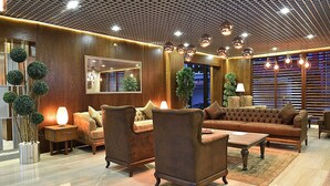Uma sala de estar moderna com um sofá, poltronas e uma mesa de centro. Há um espelho na parede e um vaso de planta.