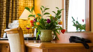 Quarto de hotel com escrivaninha de madeira, telefone, luminária e vaso com flores.