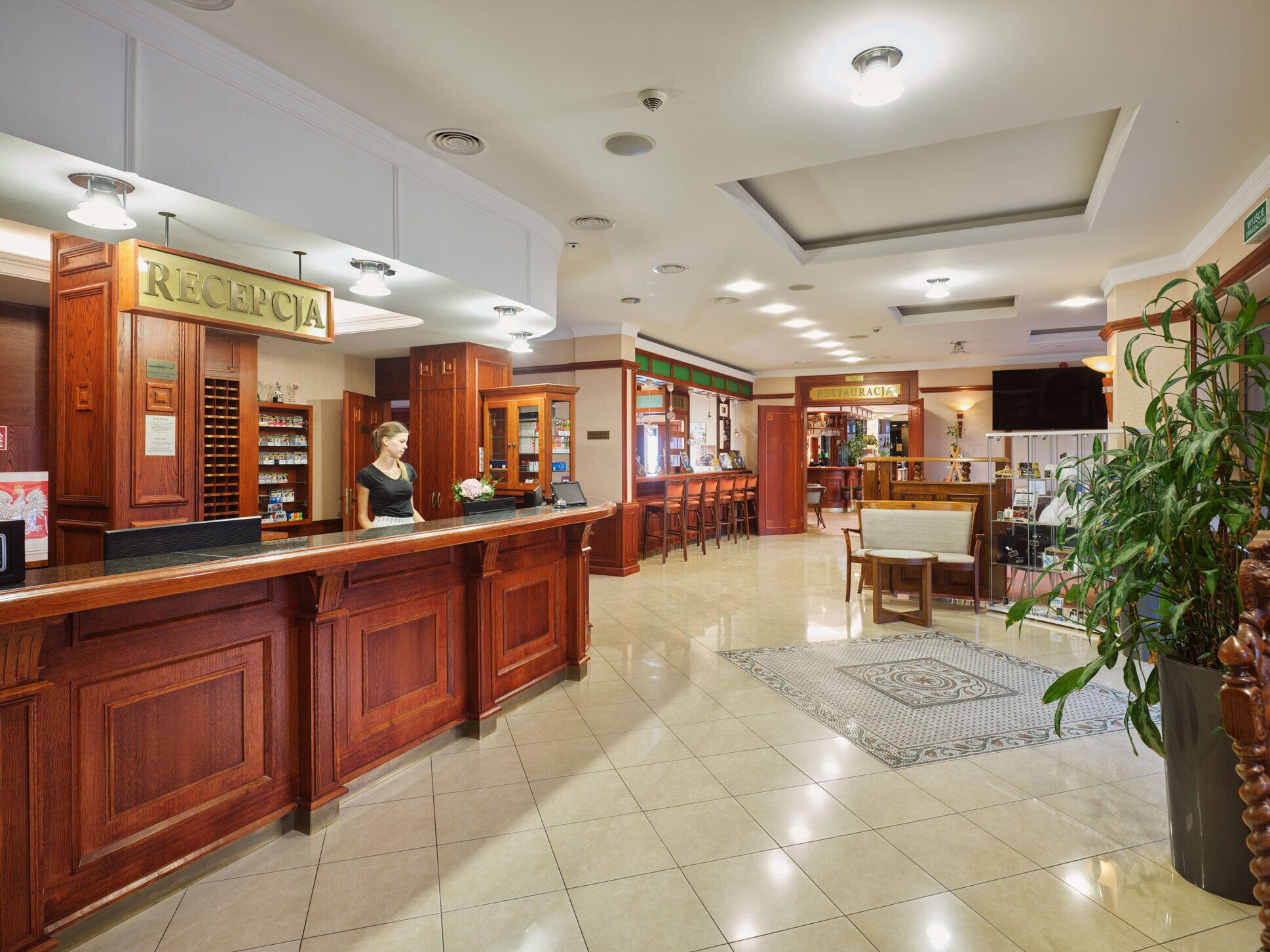 Um saguão de hotel com balcão de recepção, área de restaurante e espaço de estar com um tapete estampado.