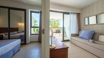 Quarto de hotel com uma cama, um sofá, uma mesa de apoio de madeira e uma porta de vidro deslizante para uma área externa com uma cadeira e uma mesa.