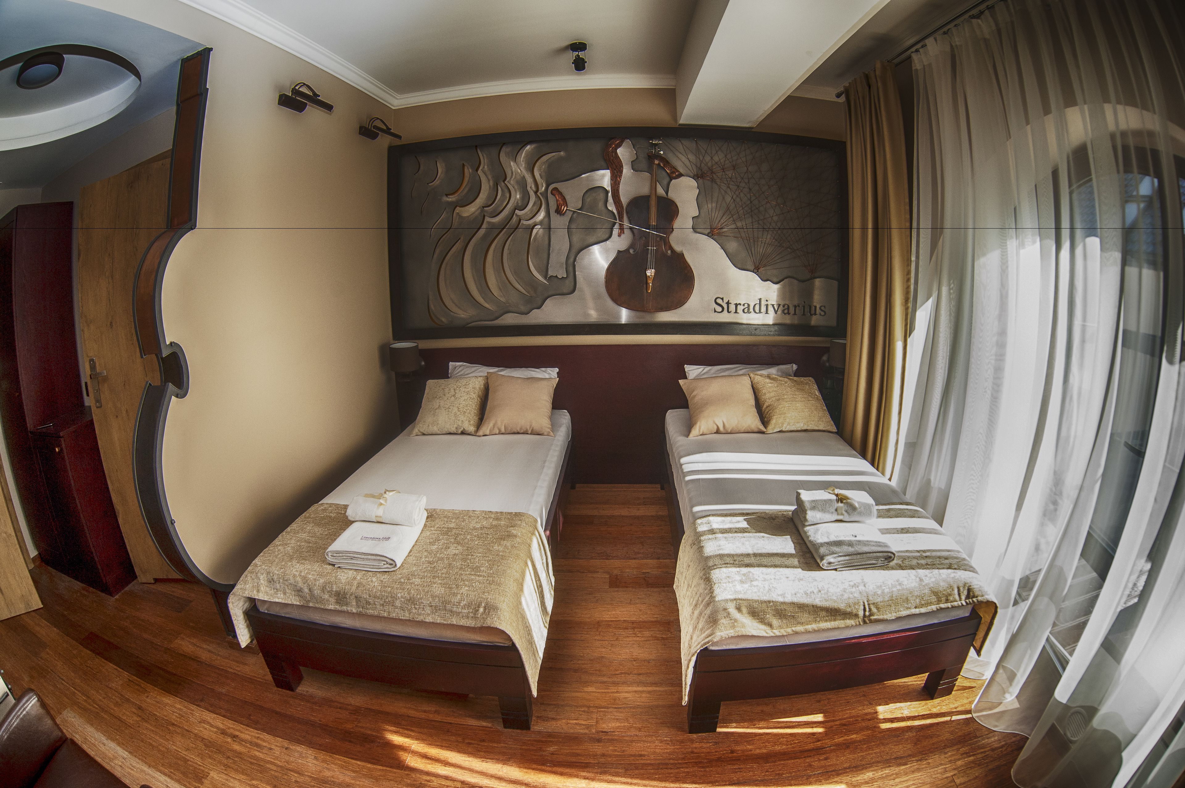 Quarto de hotel com duas camas de solteiro, um grande mural na parede com um violino e um armário de madeira curvada.