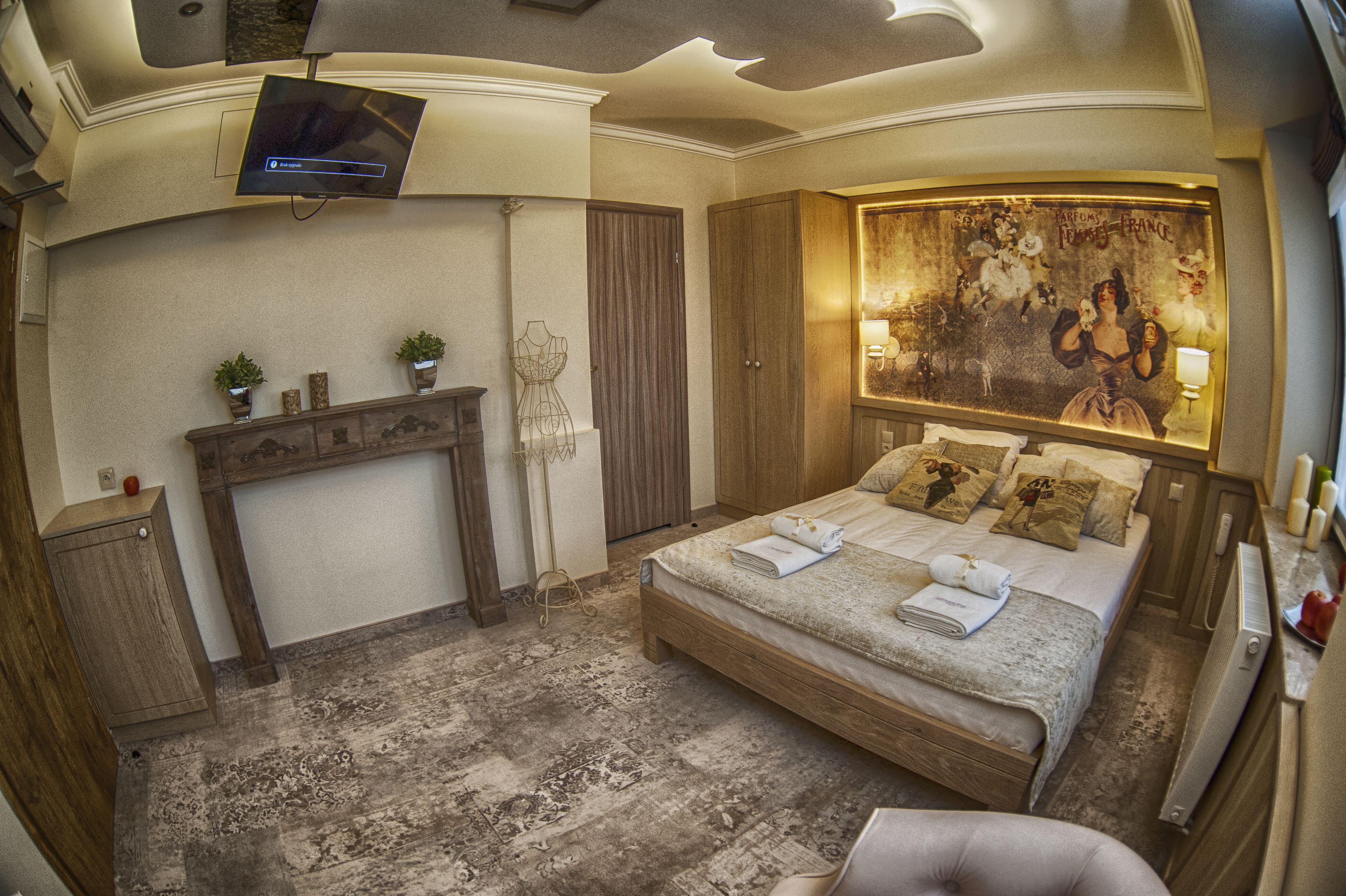 Quarto com uma cama grande, cômoda de madeira, lareira e televisão montada no teto.